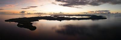 Sunrise illuminates clouds that drift over the calm waters of the ...